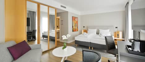 Quarto de hotel moderno com cama, escrivaninha, poltrona, sofá e uma pequena mesa com um vaso de flores.