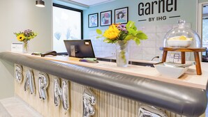 Uma área de recepção com design moderno, apresentando um balcão com um laptop, um vaso com flores e uma vitrine com cúpula de vidro.
