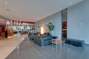 Um saguão de hotel moderno com área de estar, balcão de recepção e uma grande planta.