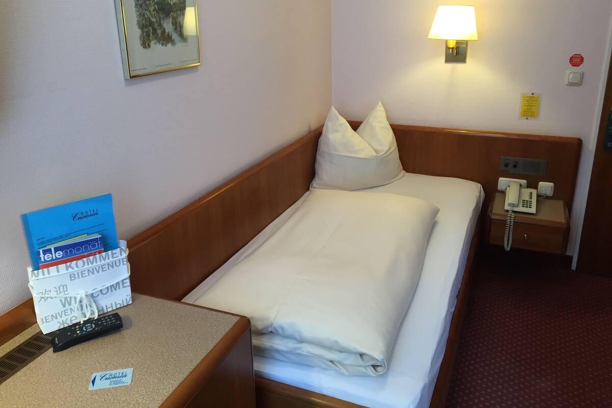 Quarto de hotel com cama bem arrumada, mesa de cabeceira com controle remoto, telefone e uma cesta de boas-vindas.