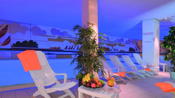 Área de piscina com espreguiçadeiras, uma mesa com frutas e uma bebida, e uma planta grande.
