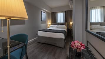 Quarto de hotel com cama, mesas de cabeceira, escrivaninha com cadeira, abajur e um vaso com flores.
