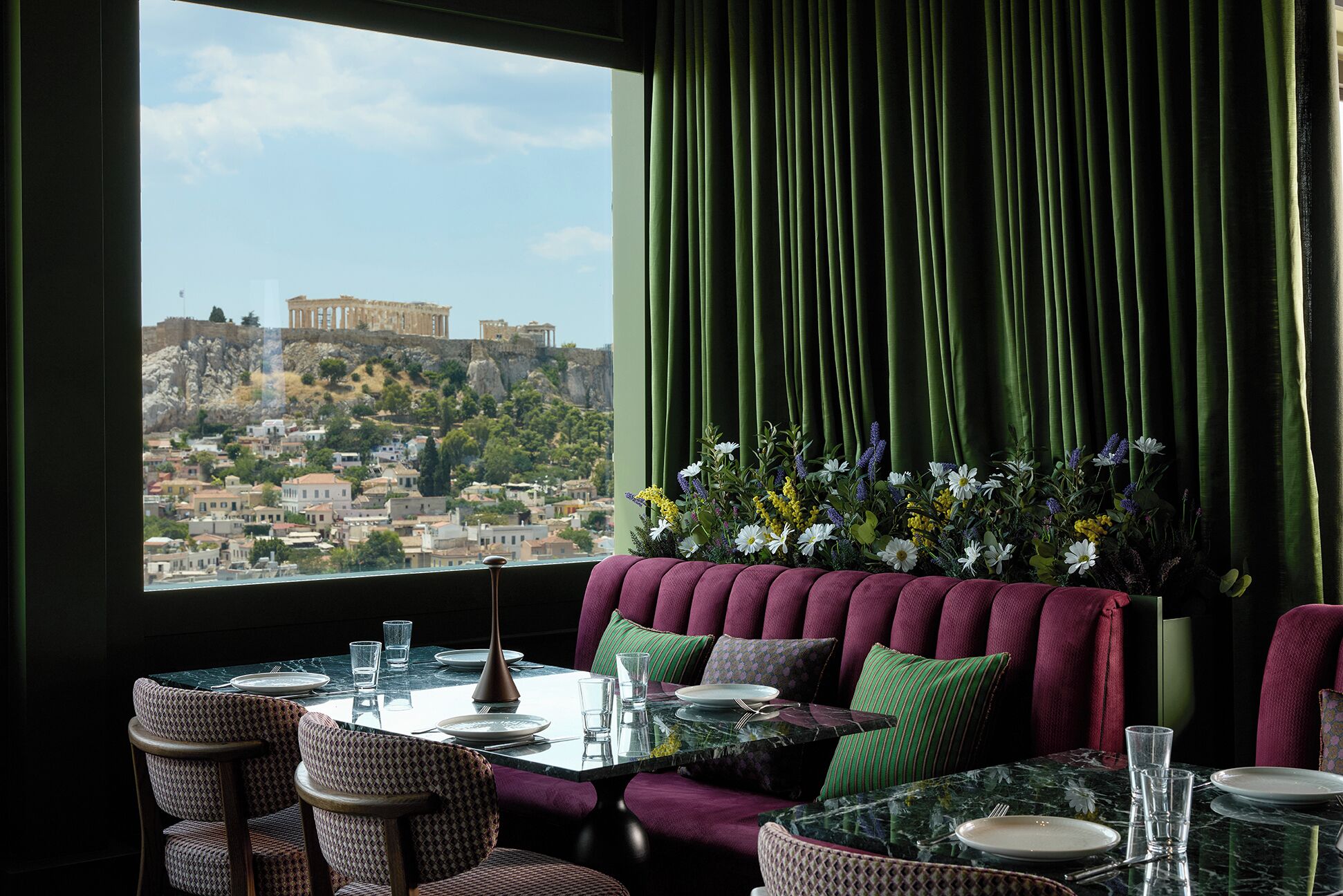 Uma área de refeições com vista para um edifício histórico, uma mesa posta com pratos e copos, e um sofá com almofadas.