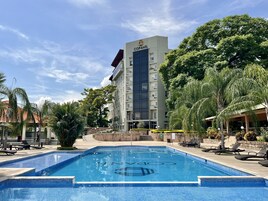 Hotel com piscina, palmeiras e um prédio grande com a sinalização 'COPANTL'.