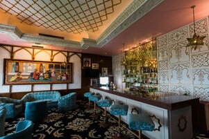 Uma área de bar com piso estampado, banquetas azuis estofadas e teto decorativo.