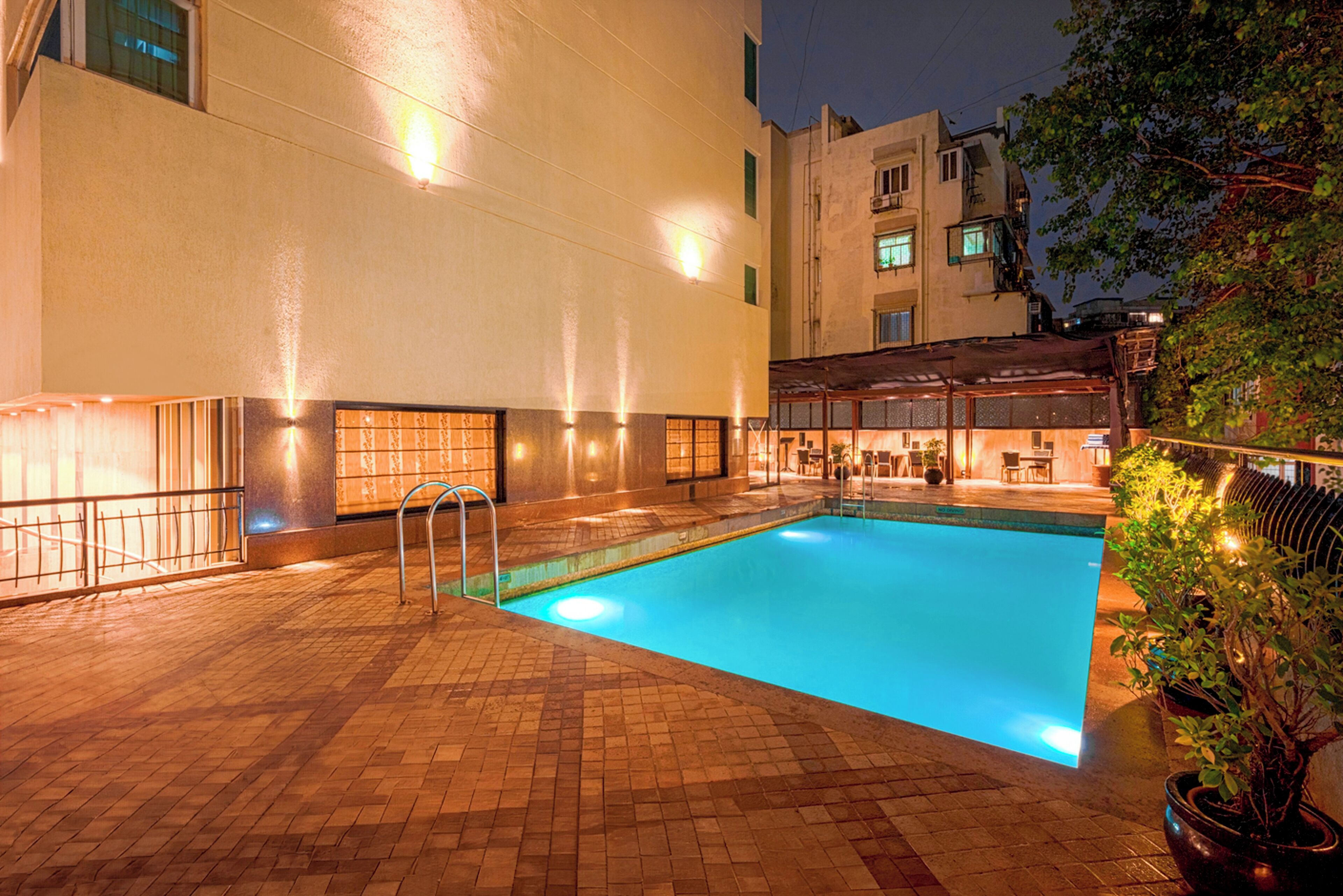 Piscina ao ar livre com deck revestido, rodeada por edifícios com janelas iluminadas.