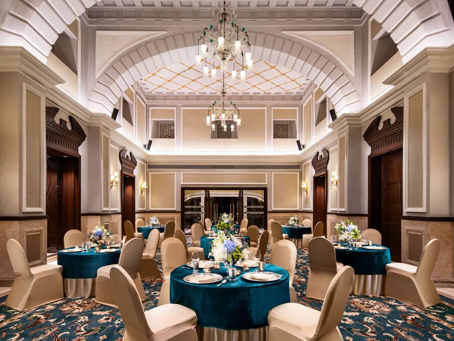 Uma sala de jantar formal com mesas redondas, cadeiras e um candelabro.