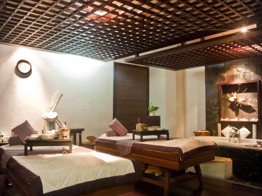Um quarto de spa com duas camas, uma mesa de massagem, lareira de pedra e um relógio fixado na parede.