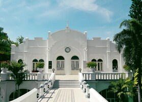 Um edifício branco com relógio, janelas em arco e entrada central.