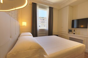 Quarto de hotel com cama grande, TV de tela plana, minibar e janela com cortinas.