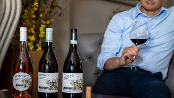Três garrafas de vinho Centovie sobre uma mesa, com uma rolha na frente. Um homem segura uma taça de vinho.