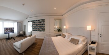 Quarto de hotel com uma cama grande, televisão, área de estar e minibar.