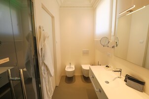 Uma casa de banho com chuveiro de vidro, sanita, bidé, lavatório com espelho e porta-toalhas.