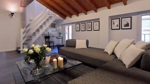 Uma sala de estar moderna com uma mesa de centro de vidro, um sofá cinza e teto de madeira.