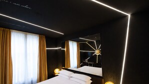 Quarto de hotel moderno com uma cama grande, um espelho e uma luminária de parede original.