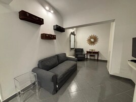Uma sala de estar moderna com um sofá cinzento, uma mesinha, uma cadeira e uma TV sobre um móvel.