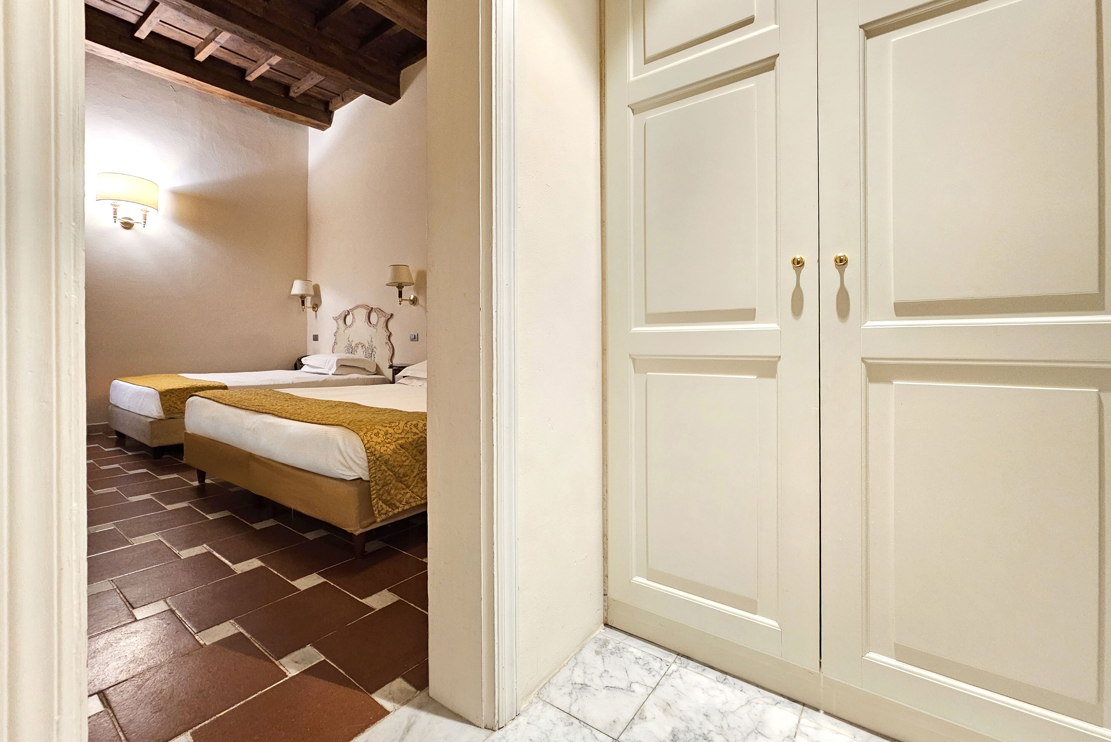 Quarto de hotel com duas camas, piso de mármore e guarda-roupa com portas duplas.