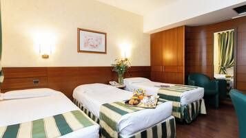 Quarto de hotel com duas camas de solteiro, área de estar com uma poltrona, escrivaninha e uma grande janela com cortinas.