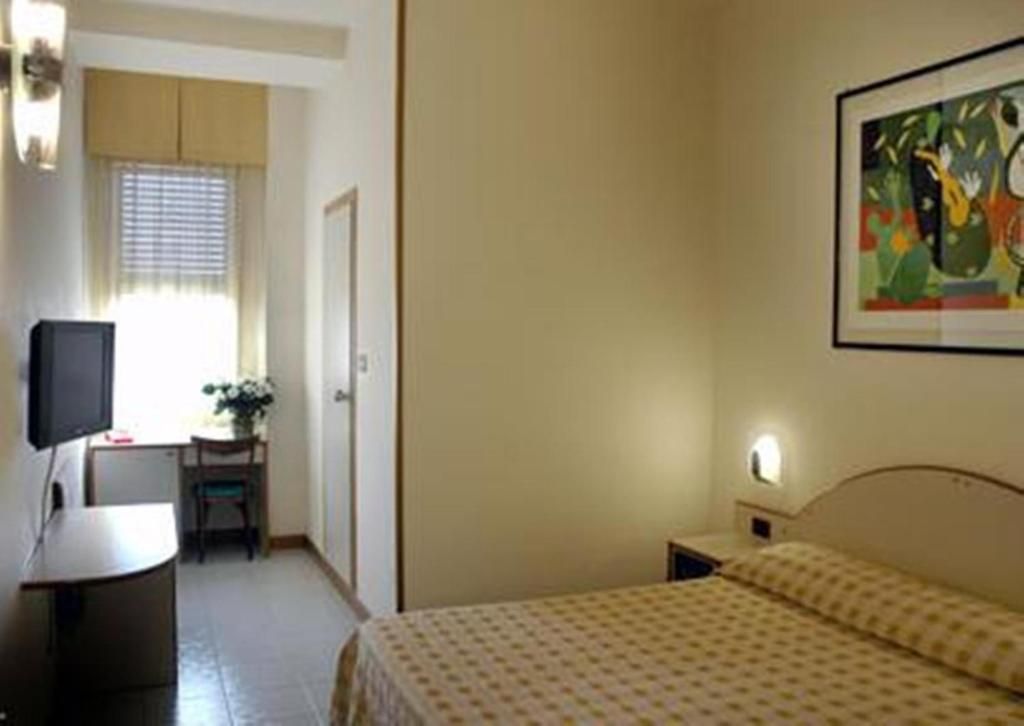 Quarto com cama, escrivaninha, cadeira e televisão.