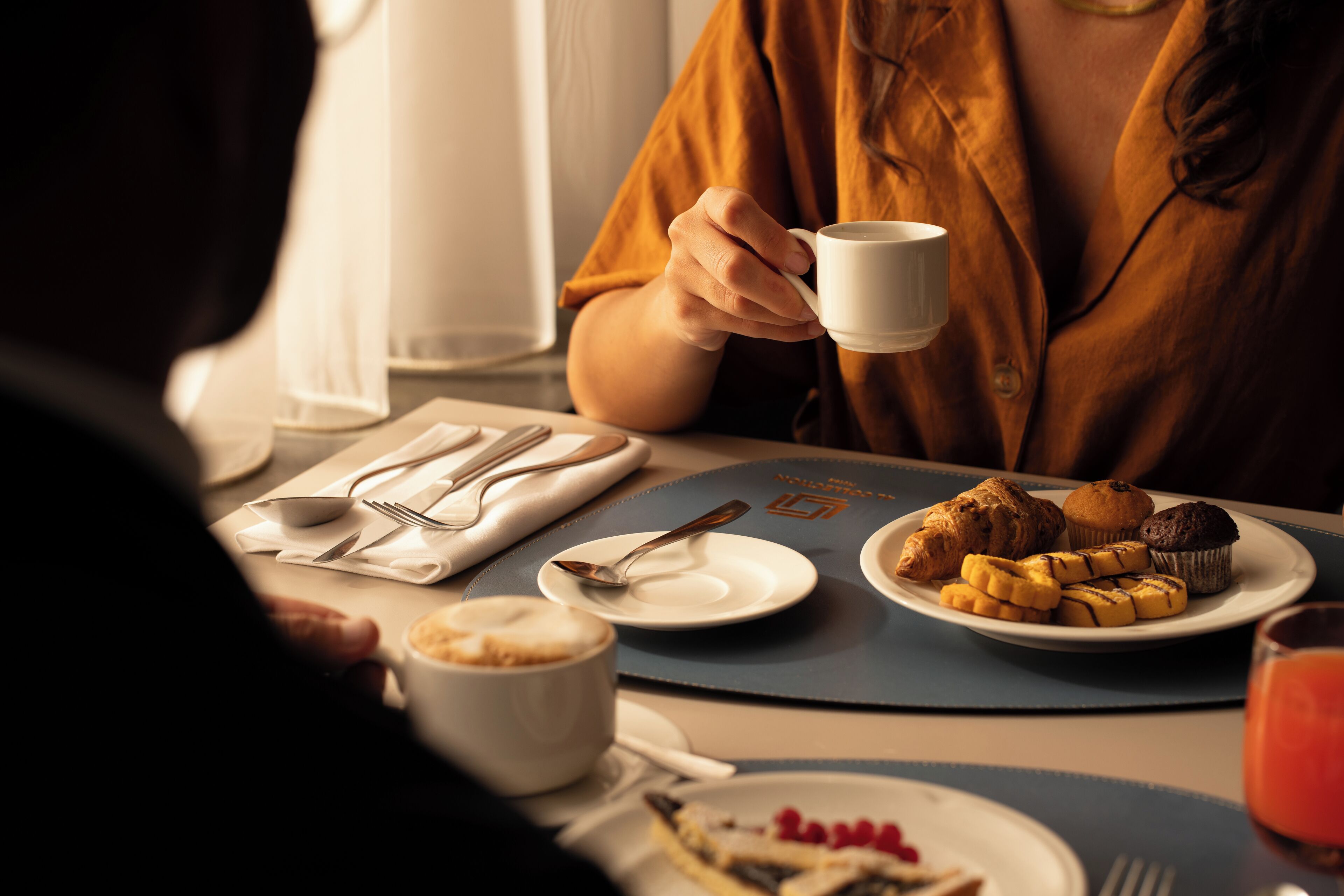 Uma mesa de jantar com um prato de doces, uma xícara de café e um copo de suco de laranja.