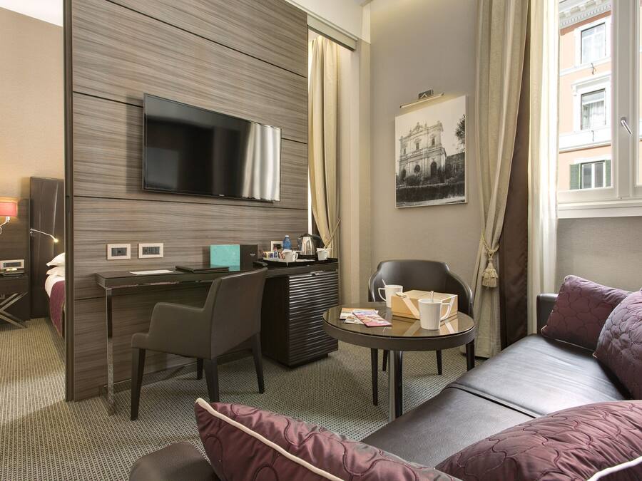Quarto de hotel moderno com cama, sofá, escrivaninha e televisão.