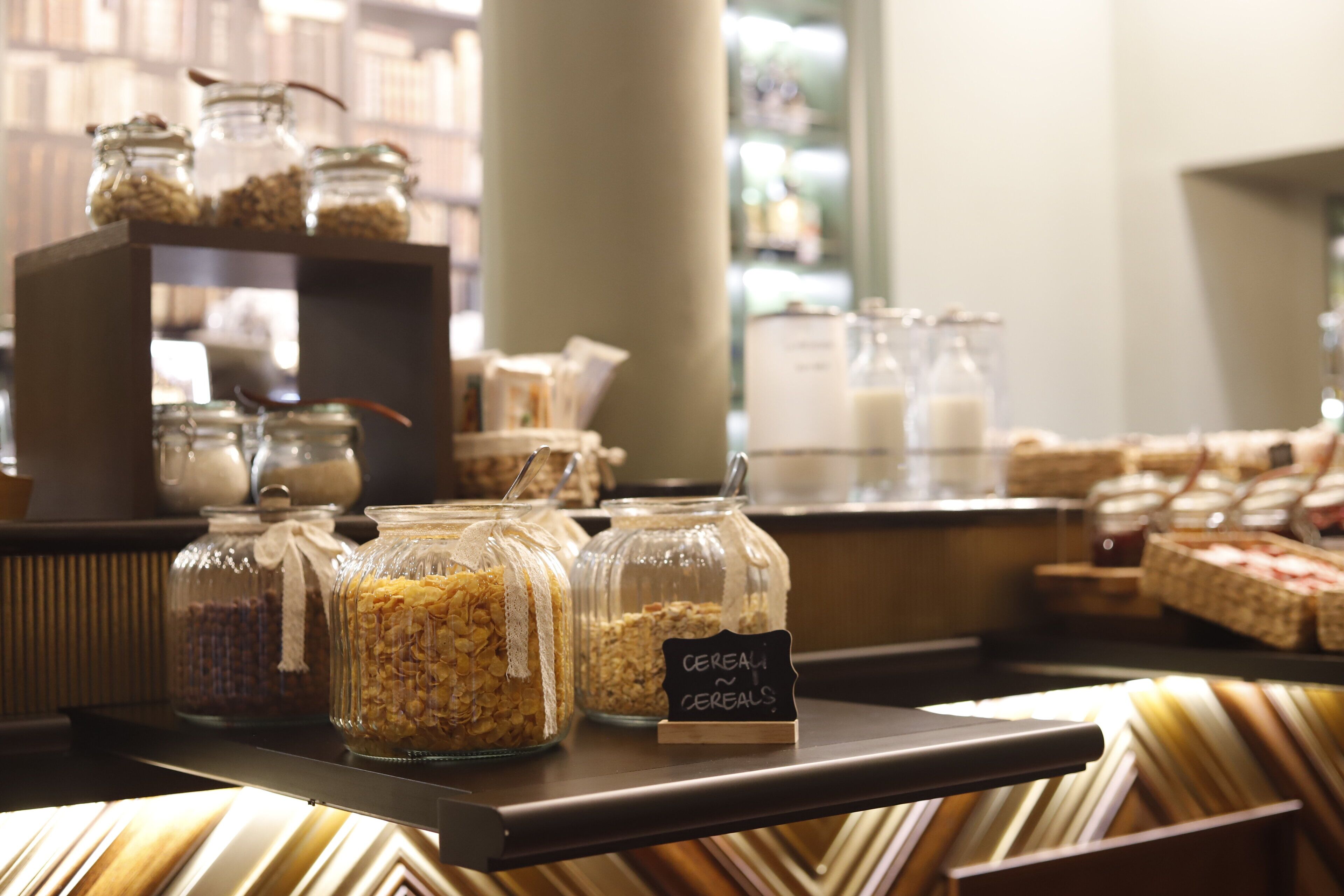 Buffet de café da manhã com diversas opções de cereais expostas em potes de vidro.