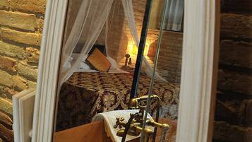 Um espelho reflete um quarto com uma cama, um aquecedor de cama em latão e uma parede com padrão de tijolos.