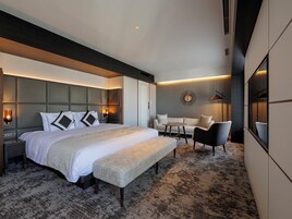 Quarto de hotel moderno com uma cama grande, um sofá, uma cadeira e uma pequena mesa.