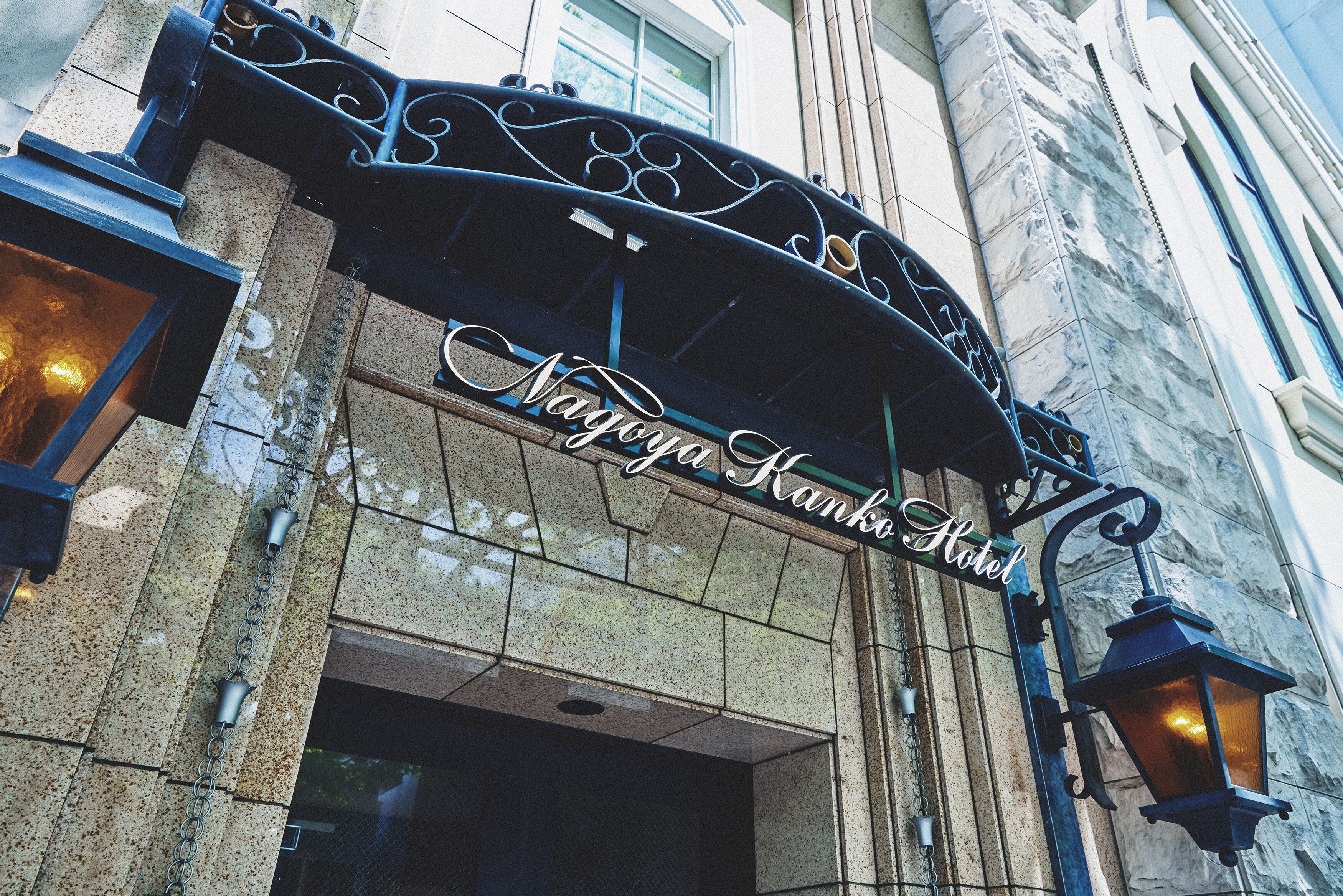 Entrada de um edifício com uma placa de ferro forjado que diz "Nagoya Kanko Hotel".