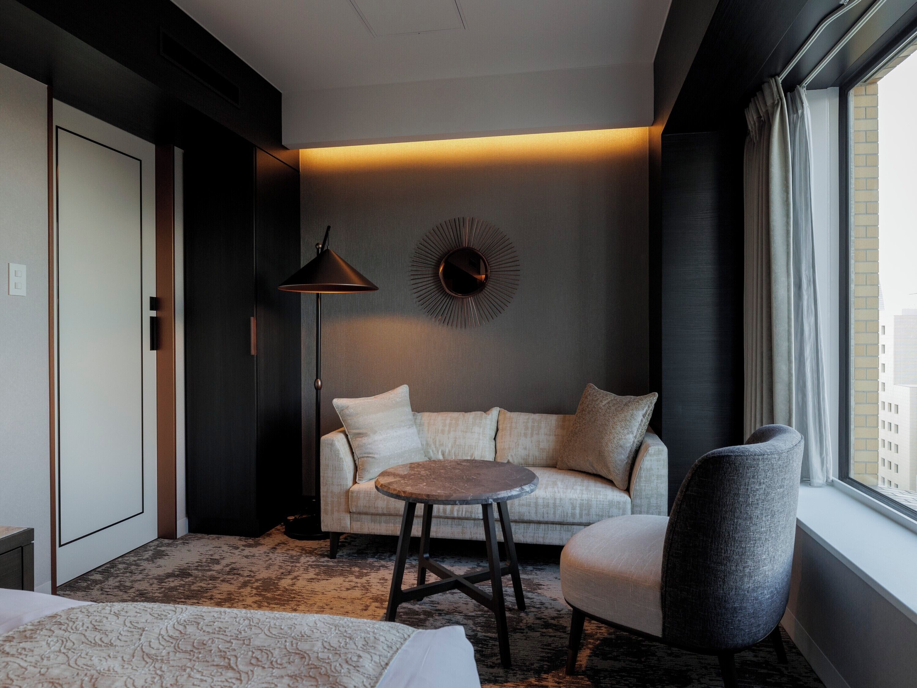 Quarto de hotel moderno com sofá, poltrona e uma pequena mesa.
