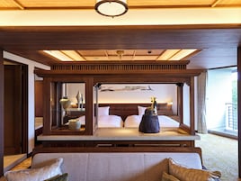 Quarto de hotel com uma cama grande, área de estar com sofá e vista para o exterior.