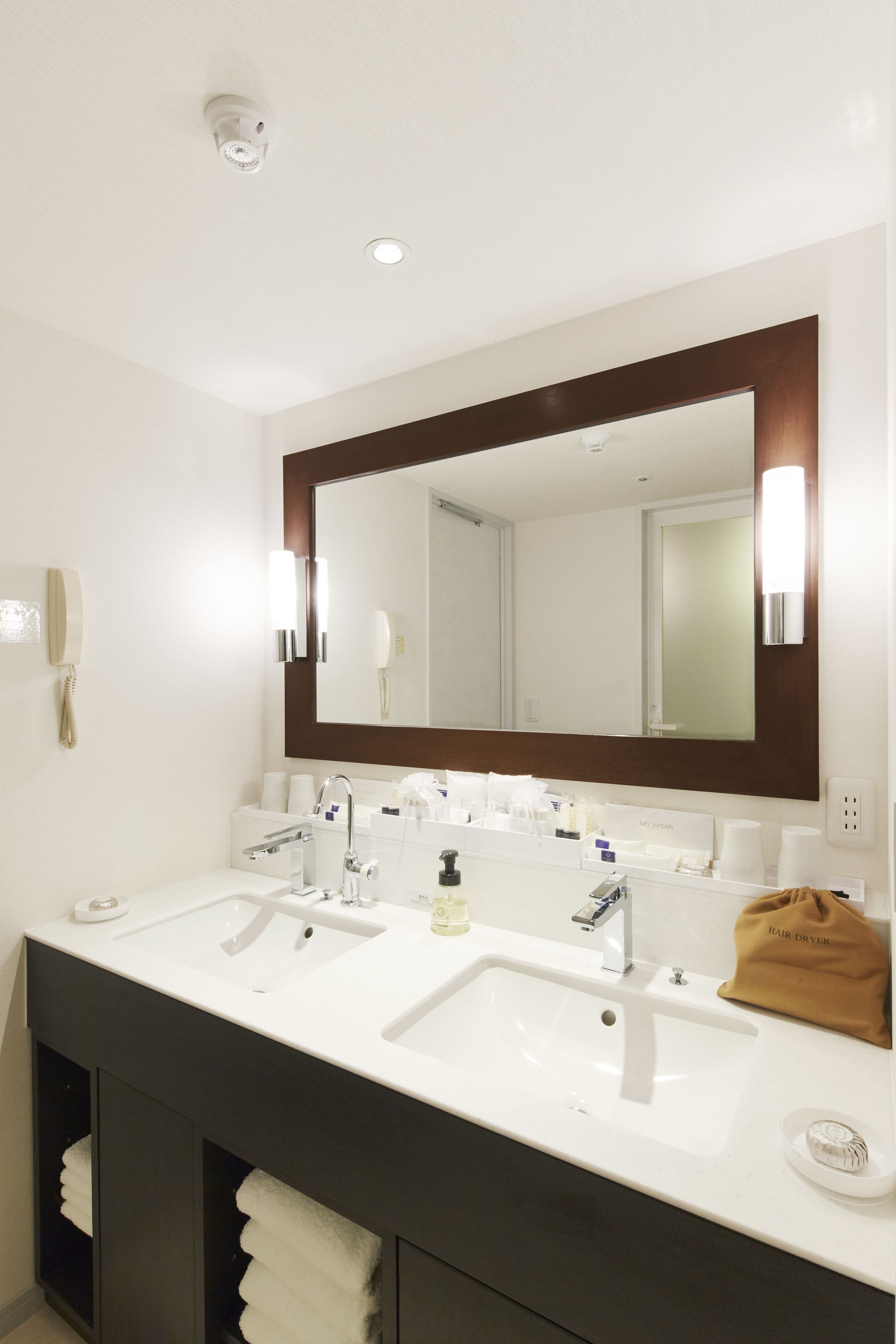 Casa de banho de hotel com duas pias, um espelho grande, um porta-toalhas e um secador de cabelo no balcão.