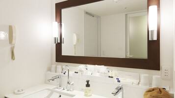 Casa de banho de hotel com duas pias, um espelho grande, um porta-toalhas e um secador de cabelo no balcão.