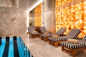Área da piscina com espreguiçadeiras, piso azulejado e parede com textura.