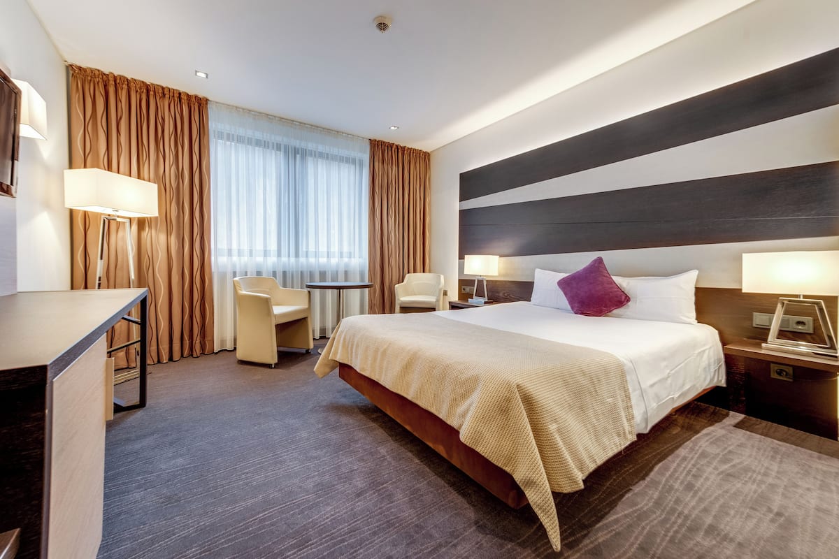 Quarto de hotel com uma cama grande, duas mesas de cabeceira, uma escrivaninha e uma cadeira.