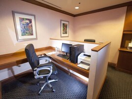 Um balcão de hotel com mesa, computador, impressora e uma cadeira.