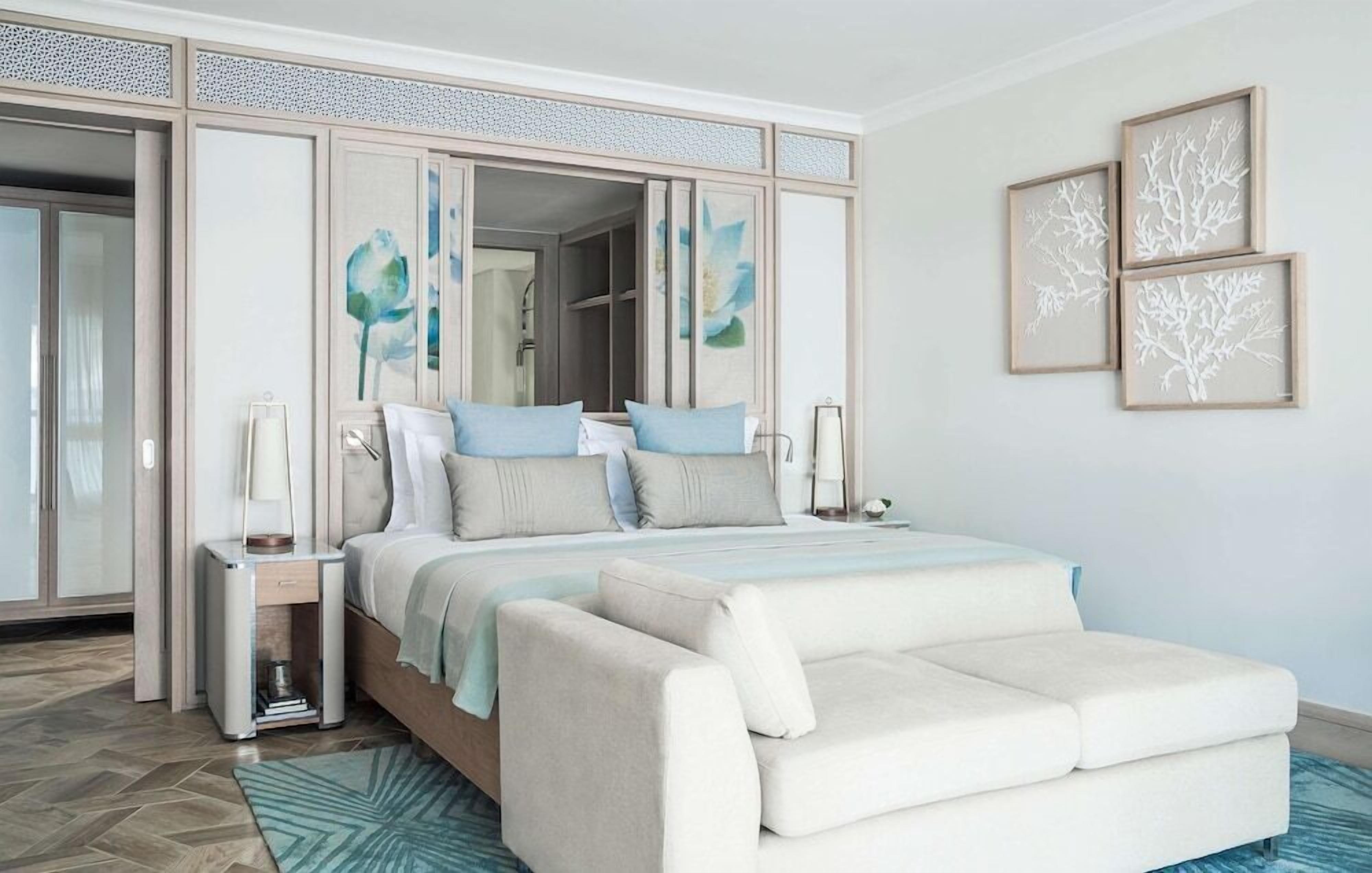Quarto com cama, mesas de cabeceira, sofá, guarda-roupa e obras de arte nas paredes.