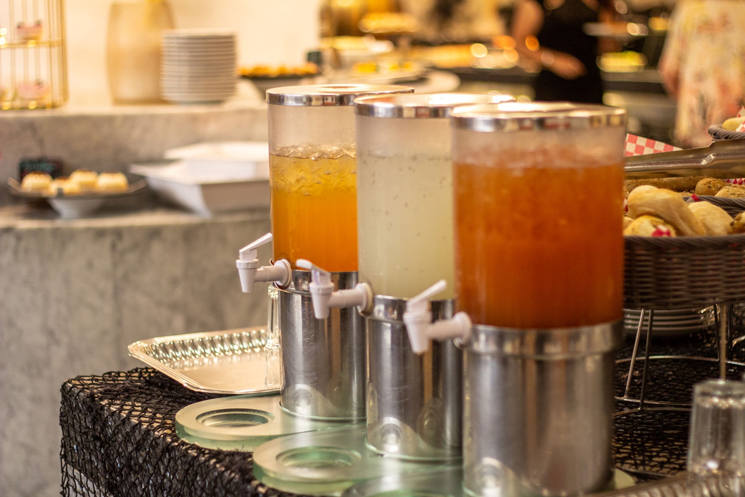Um buffet com vários dispensadores de bebidas, diversas opções de comida e uma cesta de vime.