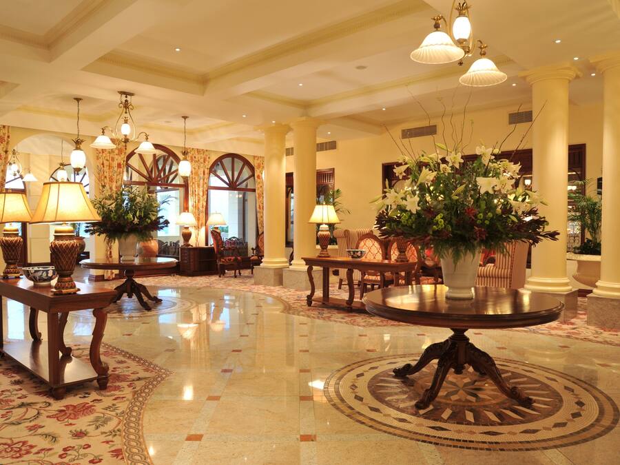 Um hall amplo com piso de mármore polido, mobiliário elegante e grandes arranjos florais.