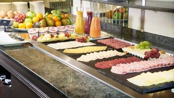 Um buffet com diversos queijos, carnes, frutas e sucos.