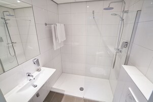 Uma casa de banho moderna com chuveiro em cabine de vidro, lavatório branco e espelho.
