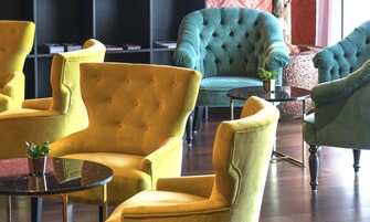 Um quarto com poltronas estofadas em amarelo e verde-água, uma mesa redonda pequena e uma estante de livros ao fundo.