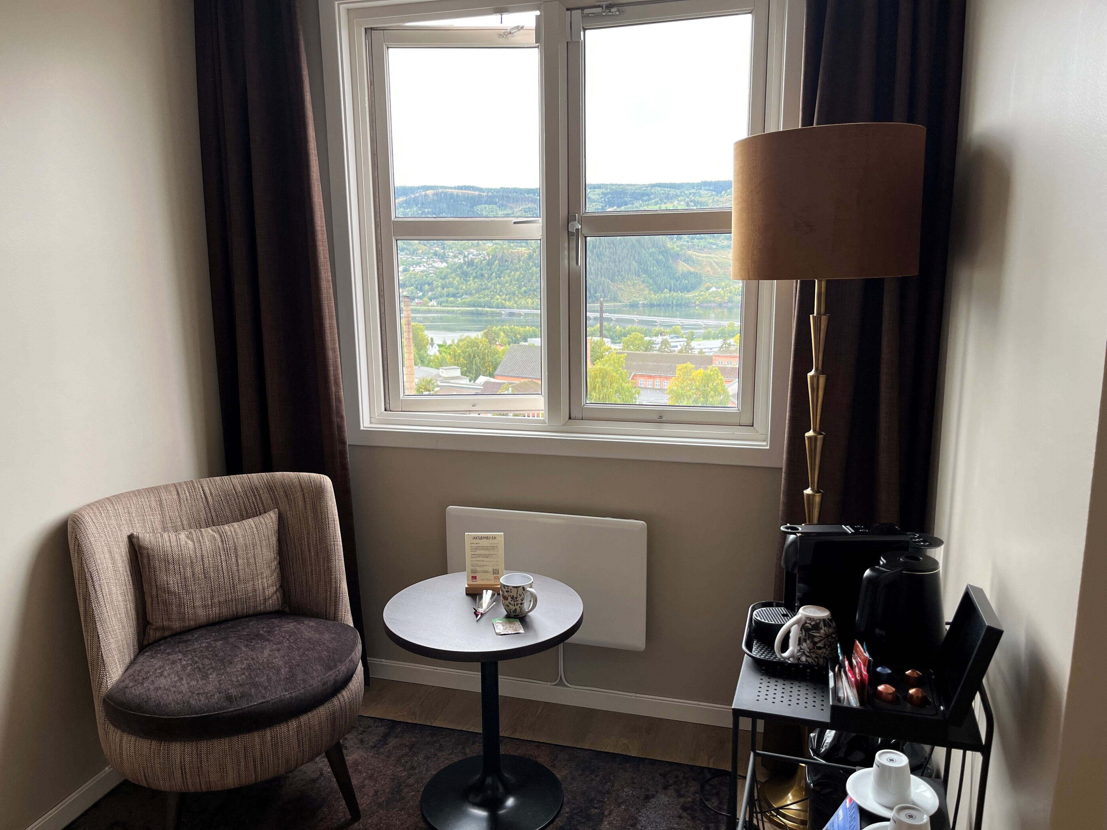 Quarto com vista para a paisagem, uma cadeira, uma mesa pequena com uma xícara e uma cafeteira.