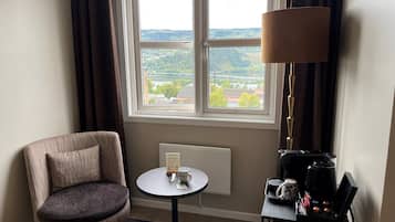 Quarto com vista para a paisagem, uma cadeira, uma mesa pequena com uma xícara e uma cafeteira.