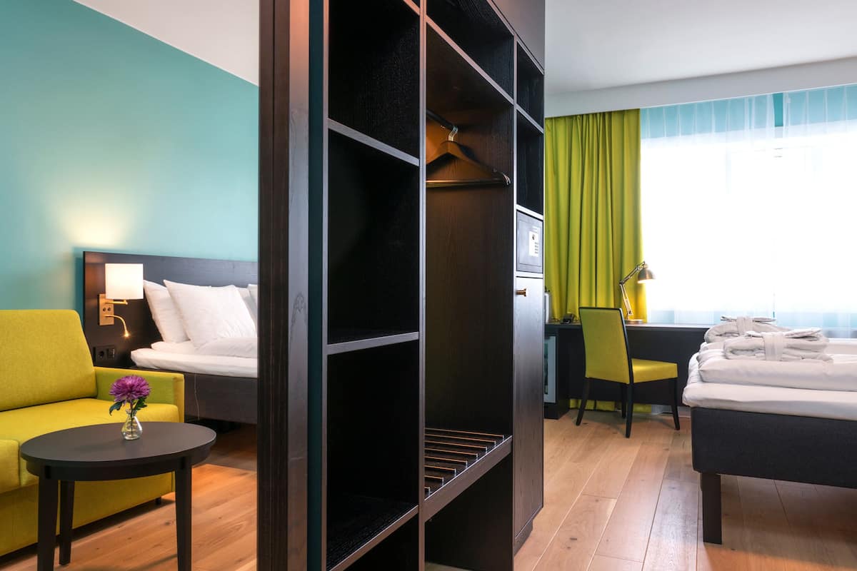 Quarto de hotel com sofá, cama, escrivaninha e uma cadeira.