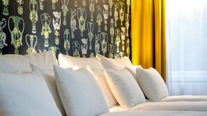 Quarto de hotel com cama, almofadas brancas e parede com design estampado.