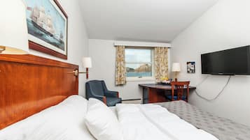 Quarto de hotel com uma cama, uma escrivaninha com cadeira, uma televisão e uma janela com cortinas.