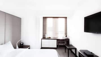 Quarto de hotel moderno com cama, escrivaninha, cadeira e televisão.