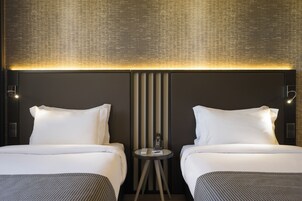 Quarto de hotel com duas camas, uma mesinha com um telefone e uma parede com textura.