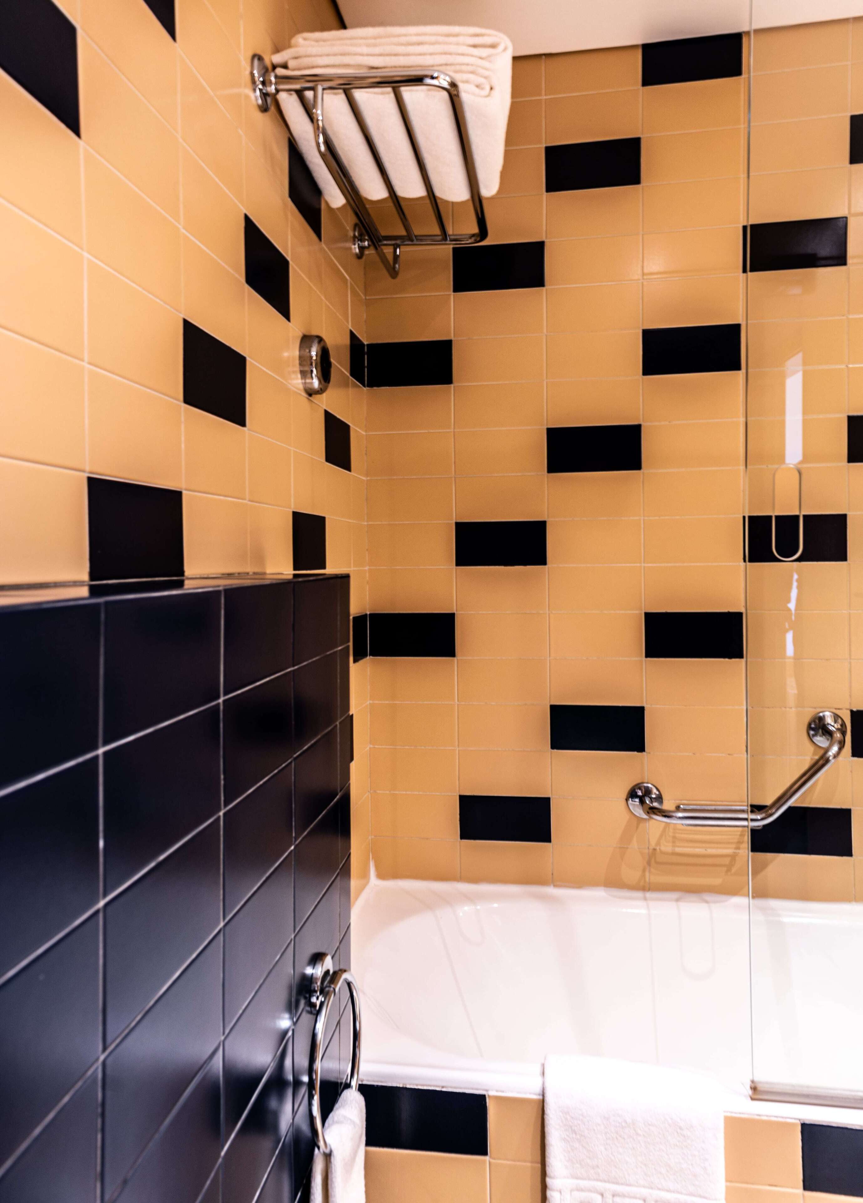 Casa de banho com parede em azulejos preto e bege, uma banheira branca e uma barra de apoio.